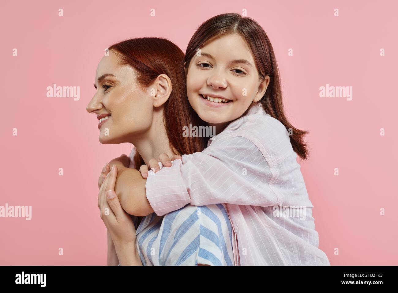 cheerful teenage girl embracing stylish mother smiling on pink backdrop ...