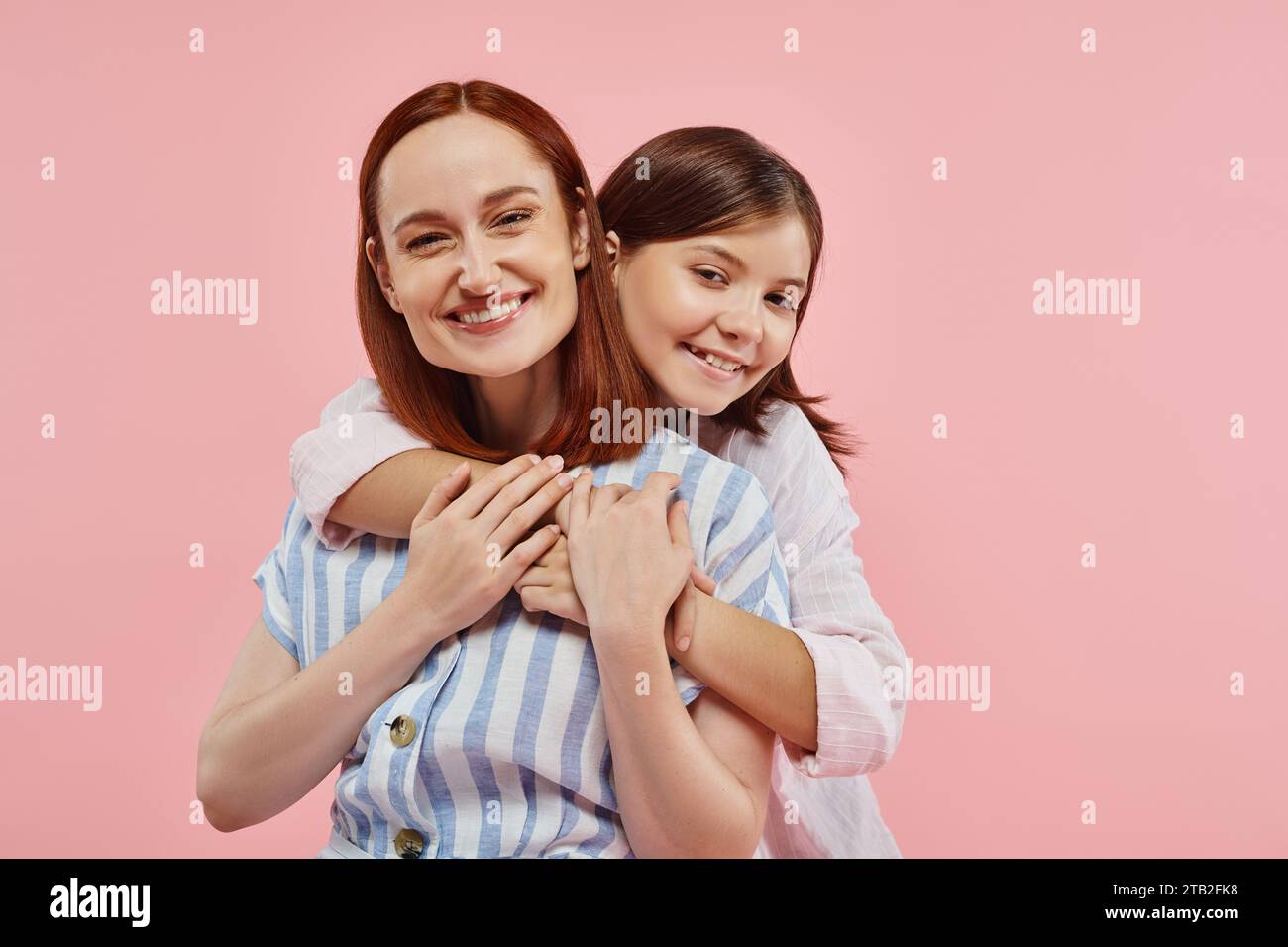 cheerful teenage girl embracing stylish mother smiling on pink backdrop ...
