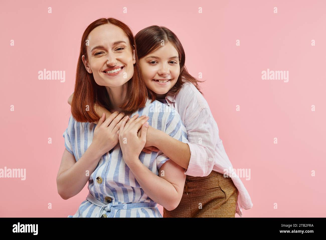 cheerful teenage girl embracing stylish mother smiling on pink backdrop ...