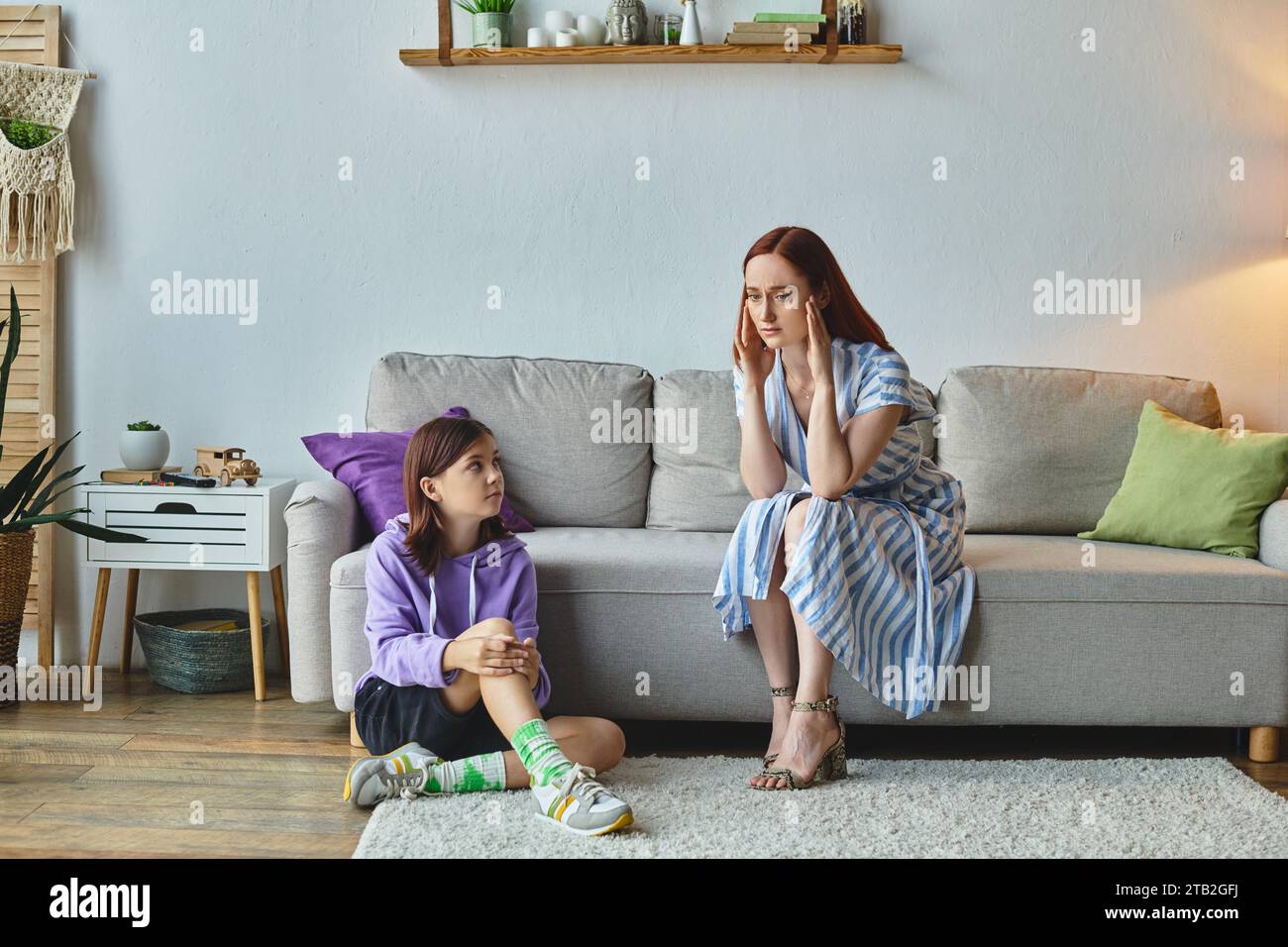 frustrated woman touching head near teenage daughter sitting on floor ...