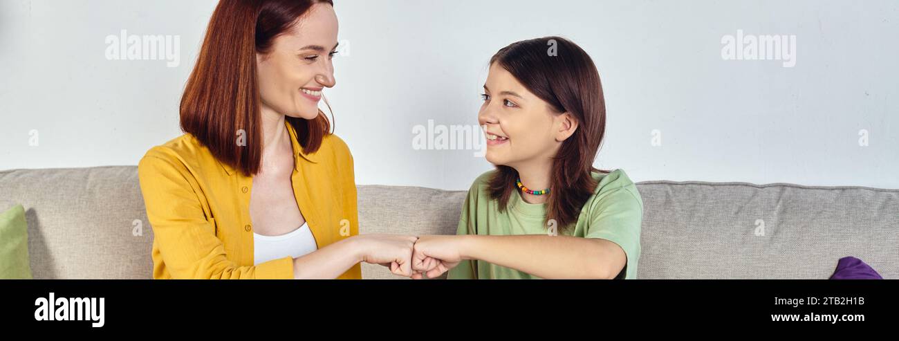 cheerful woman with teenage daughter doing fist bump on couch in living ...
