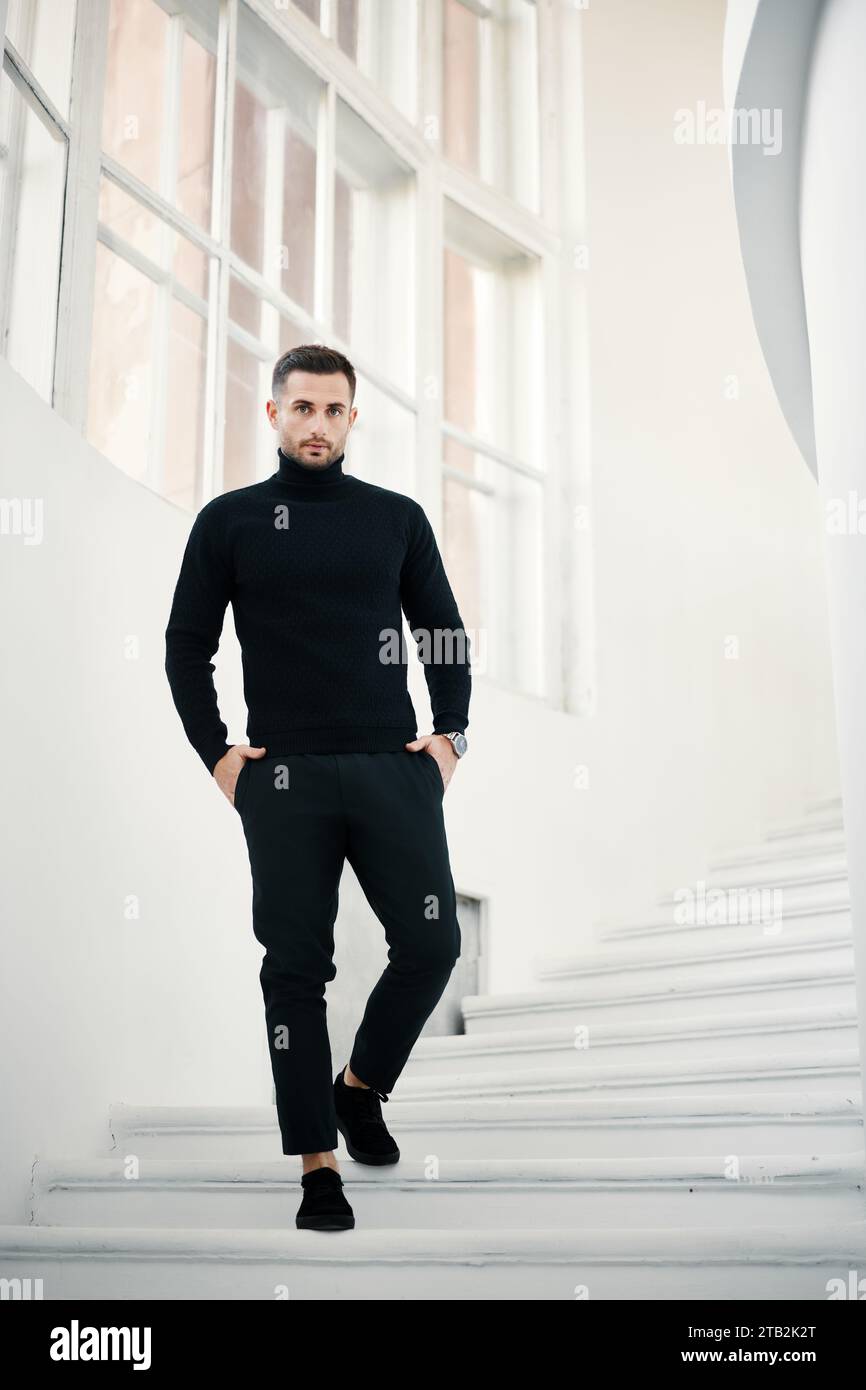 Fashionable man in a sleek black turtleneck descends a white modern ...