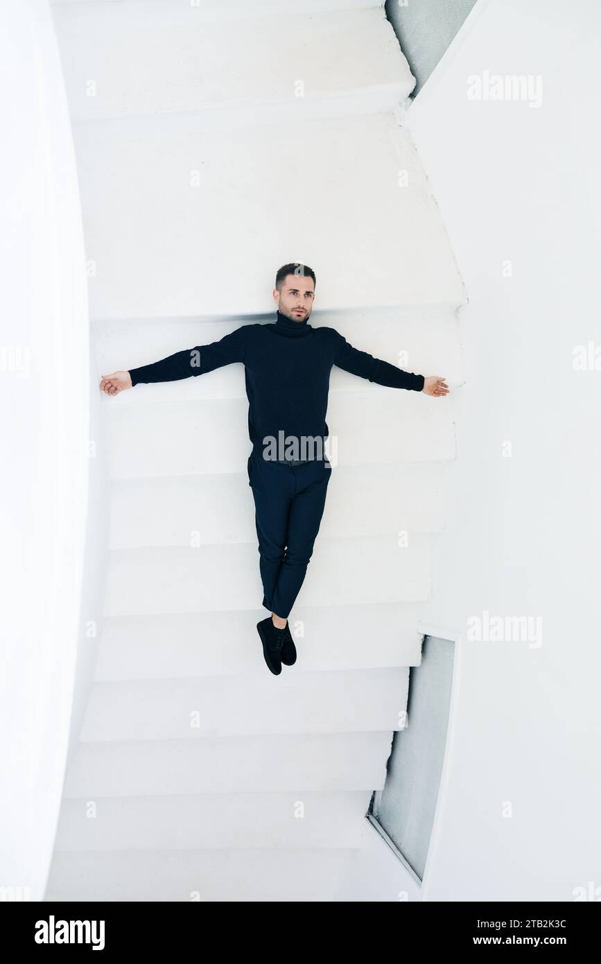 Handsome man in a black outfit lying with outstretched arms on a white ...