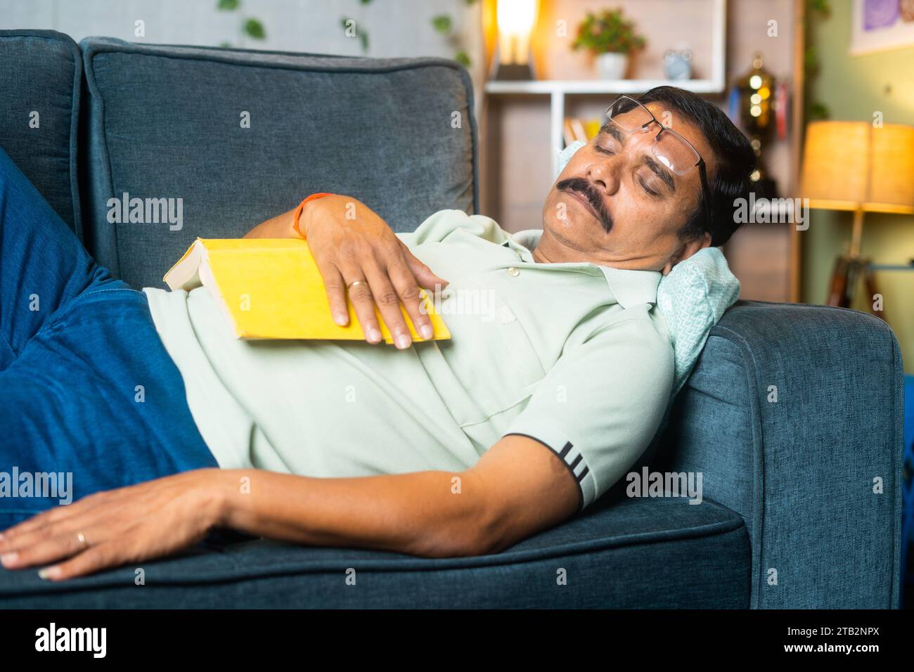 Middle aged man fallen sleep while reading book or novel on sofa at ...