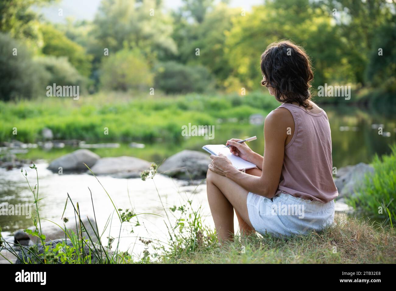A brunette woman writing near the river Stock Photo - Alamy