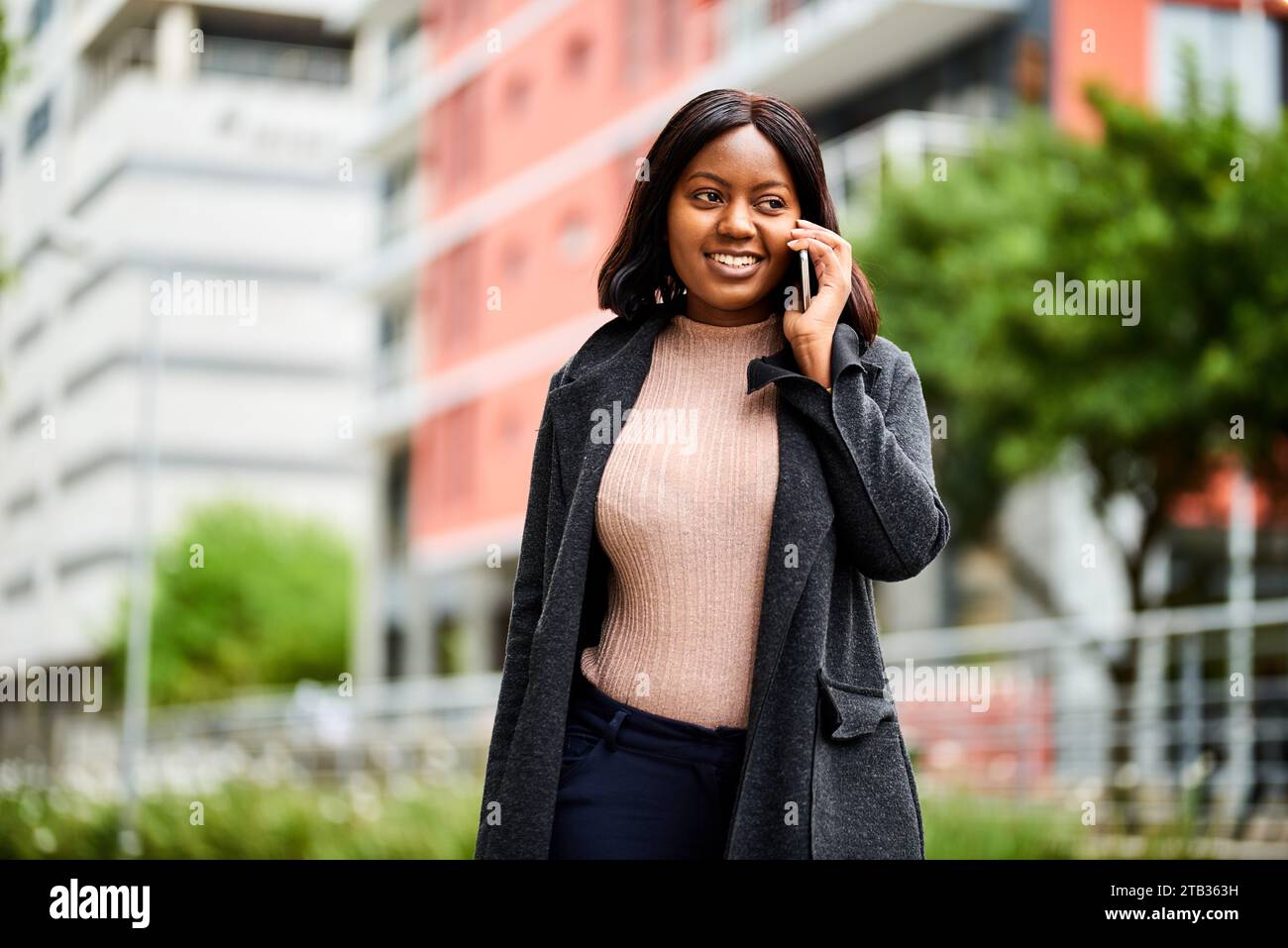 Young Black woman in formal wear making a phone call while walking ...