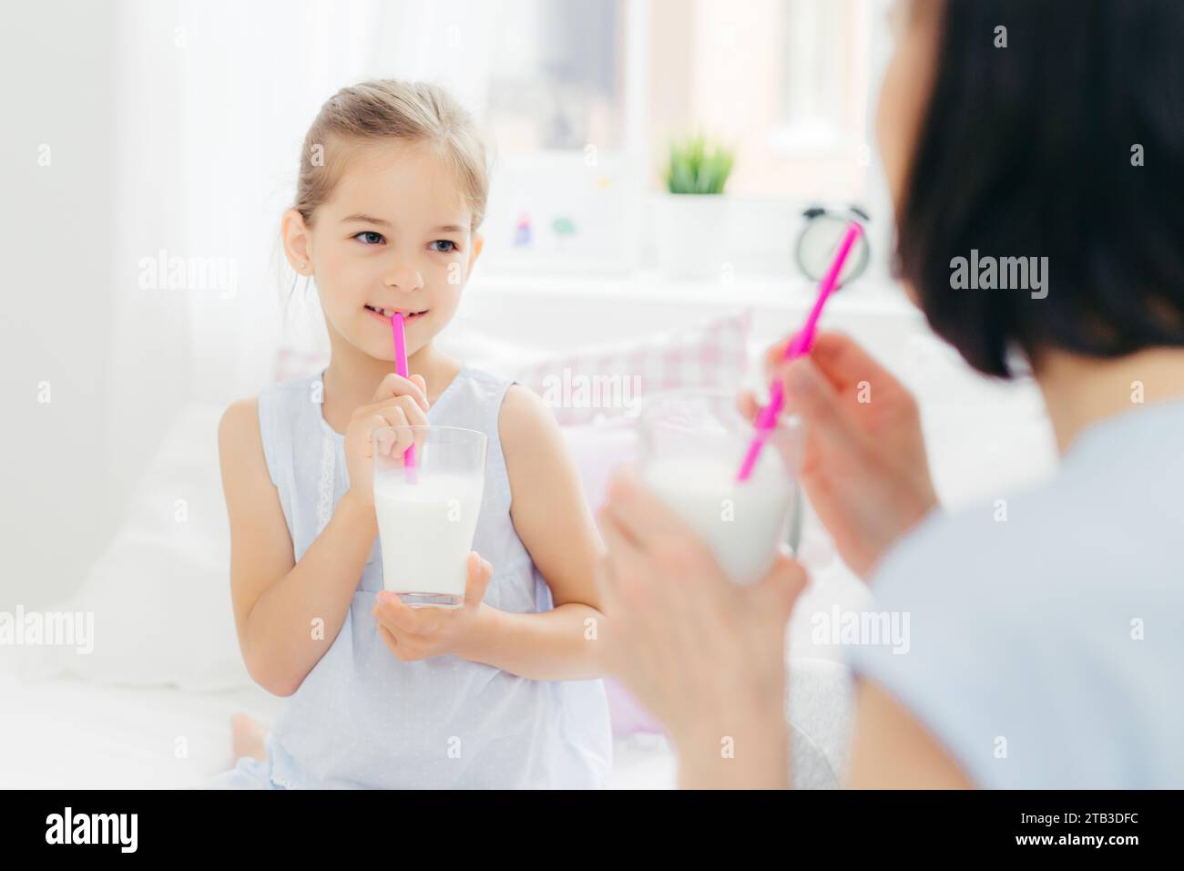 Mother and daughter sipping milk with straws, sharing a light-hearted ...
