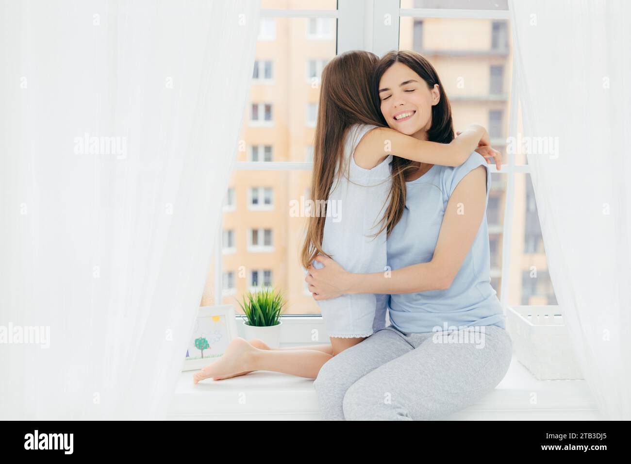Mother and daughter sharing a warm hug by the window, radiating love ...