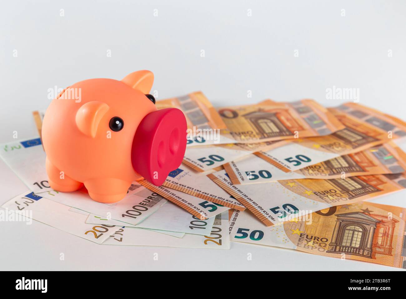 A pink pig piggy bank stands on a table covered with large quantity of ...