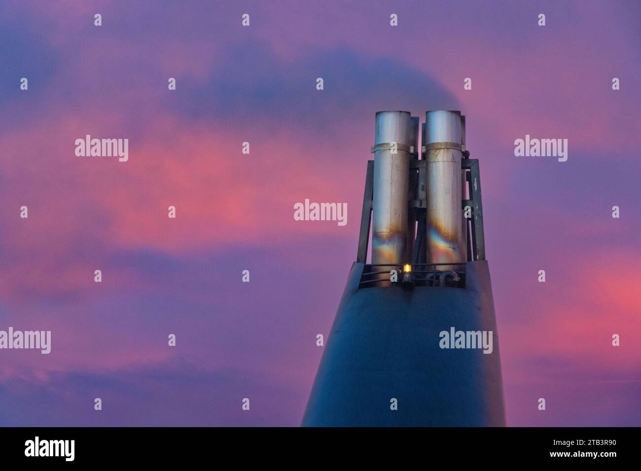 Big metallic funnel in the stern of a ship with smoke and pink sunset ...