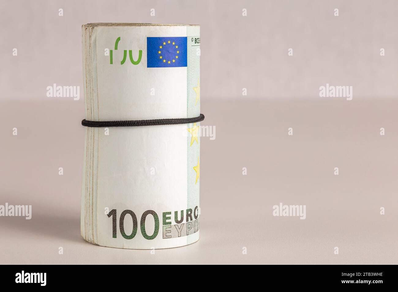 A roll of one hundred euro banknotes stands on a table on a light ...
