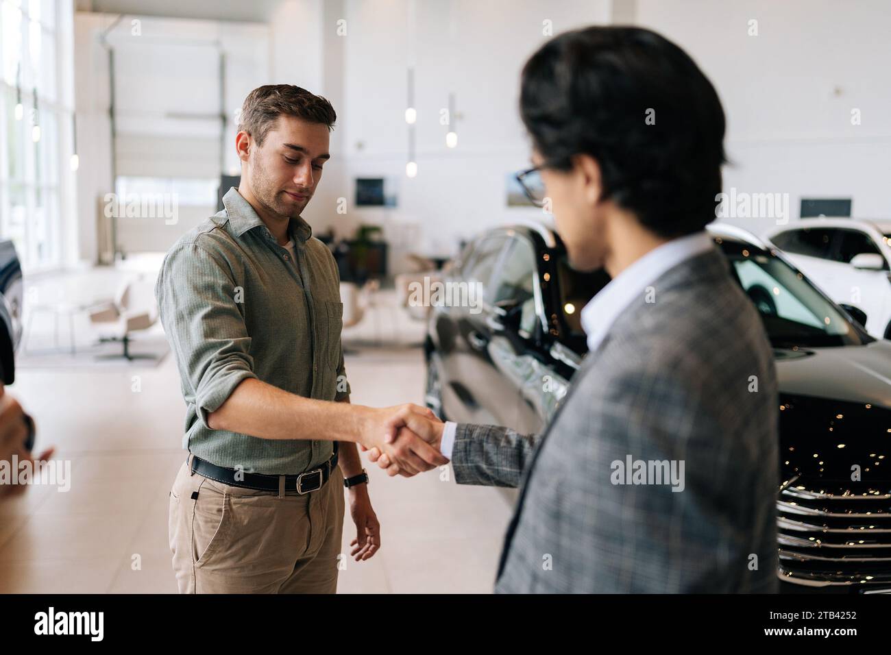Rear view of unrecognizable car dealer in business suit welcoming ...