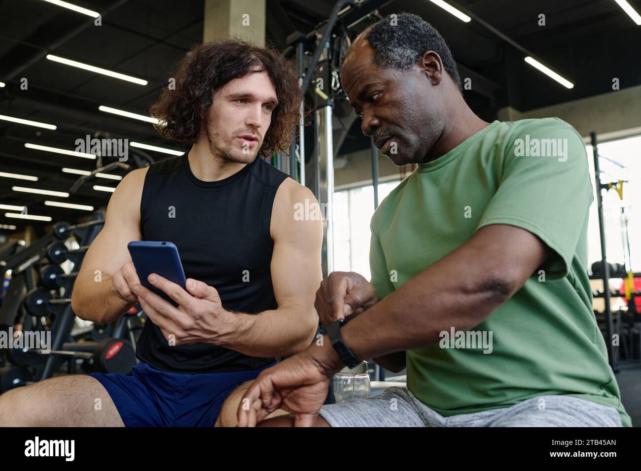 Young caucasian sportsman holding smartphone talking to senior black ...