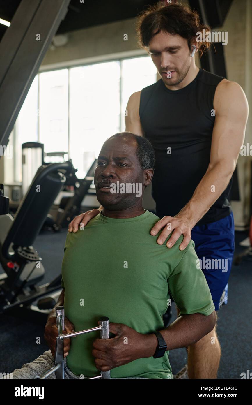 Senior black man pulling weight at gym with guidance of young caucasian ...