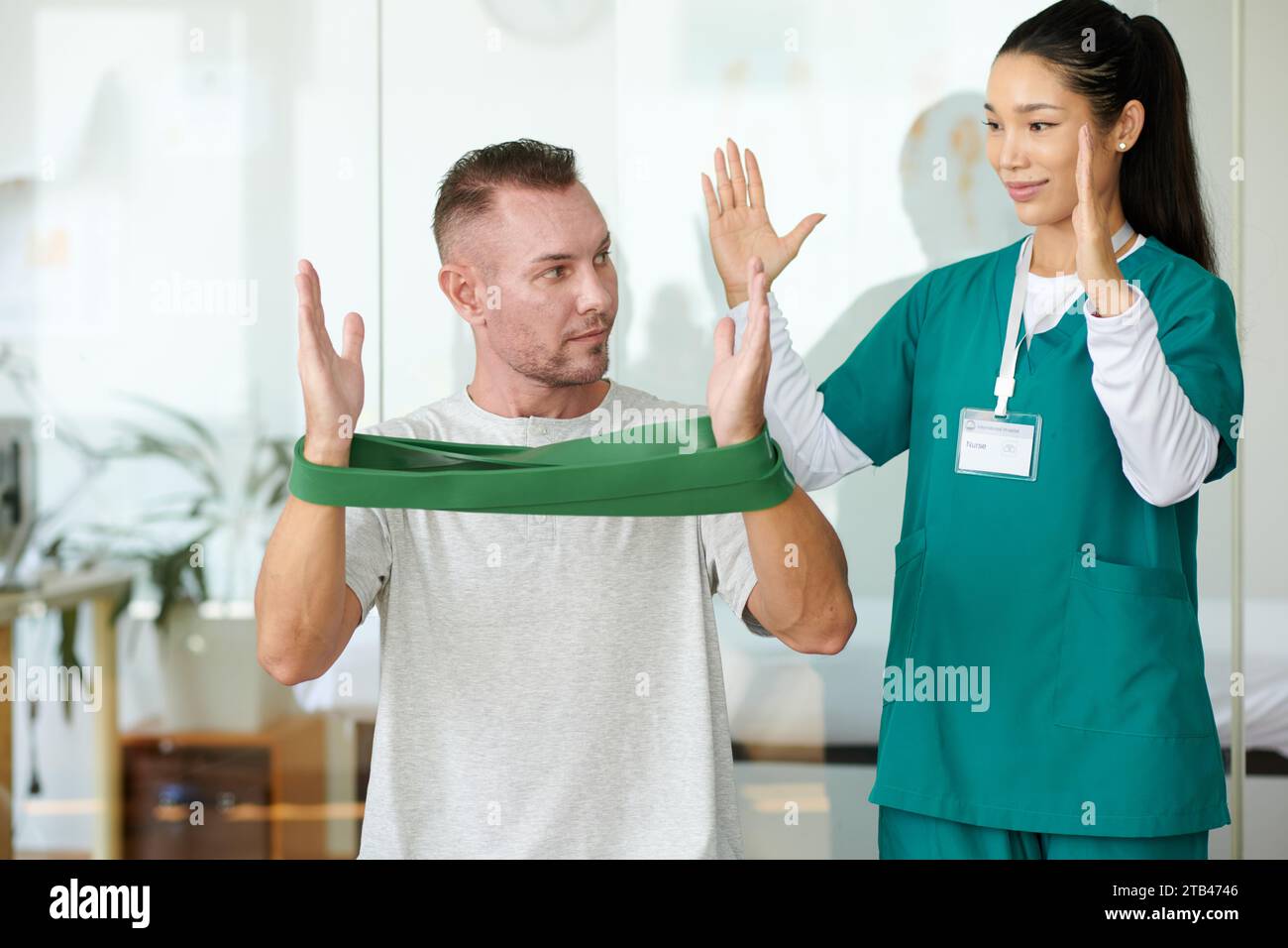 Rehab nurse showing patient how to do arm exercise with resistance band ...