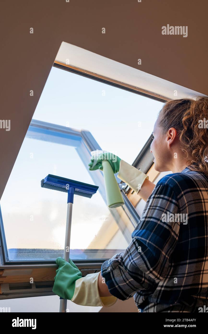 Rear view of woman cleans skylight window in her apartment. Housework ...