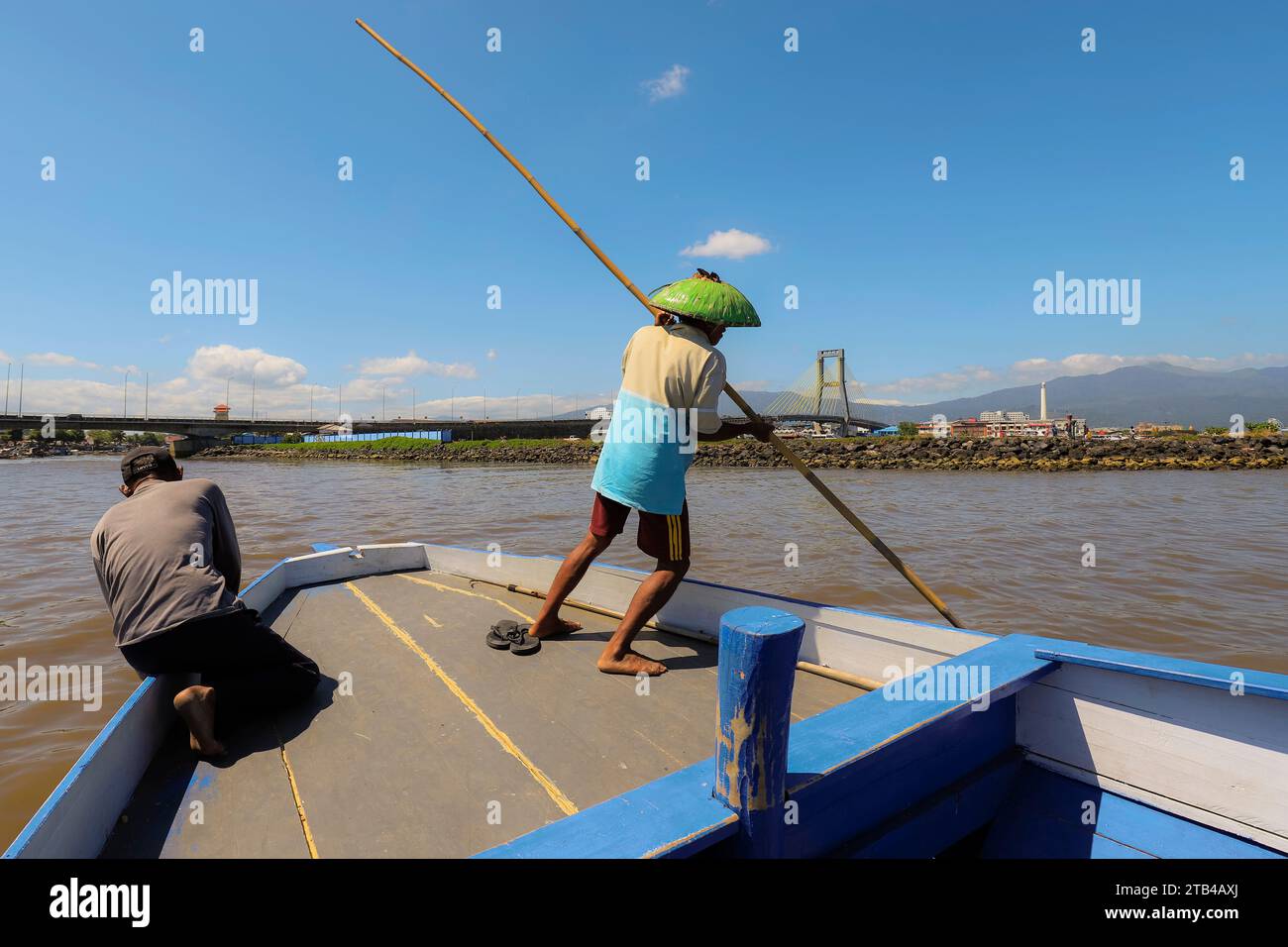 Man in bamboo hat pushes a stuck ferry off a sandbank with a pole ...