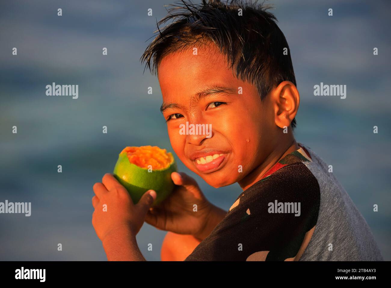 Local boy eating a ripe mango on the town pier at this coral fringed ...