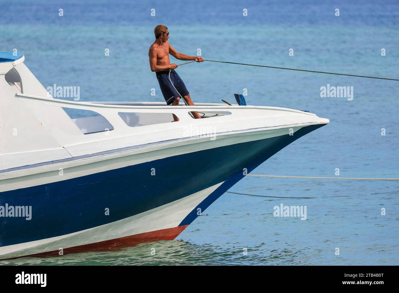 Crewman pulling rope on boat moored with the mainland beyond, off this ...