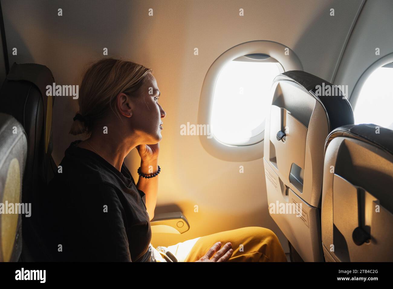 Passenger woman is flying in plane. Girl sitting in airplane looking ...