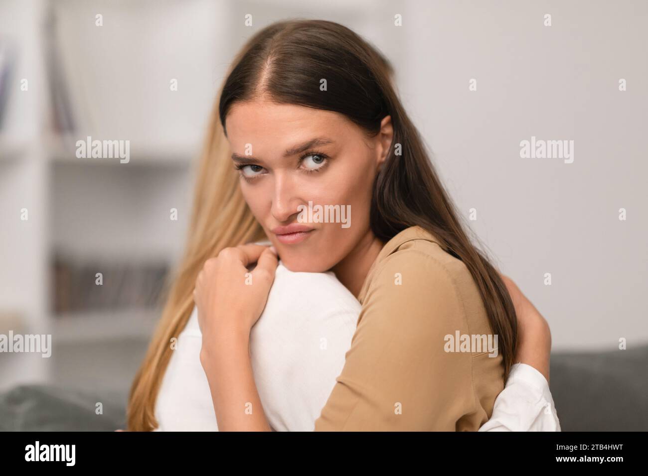 Annoyed young lady embracing her girlfriend with displeased expression ...