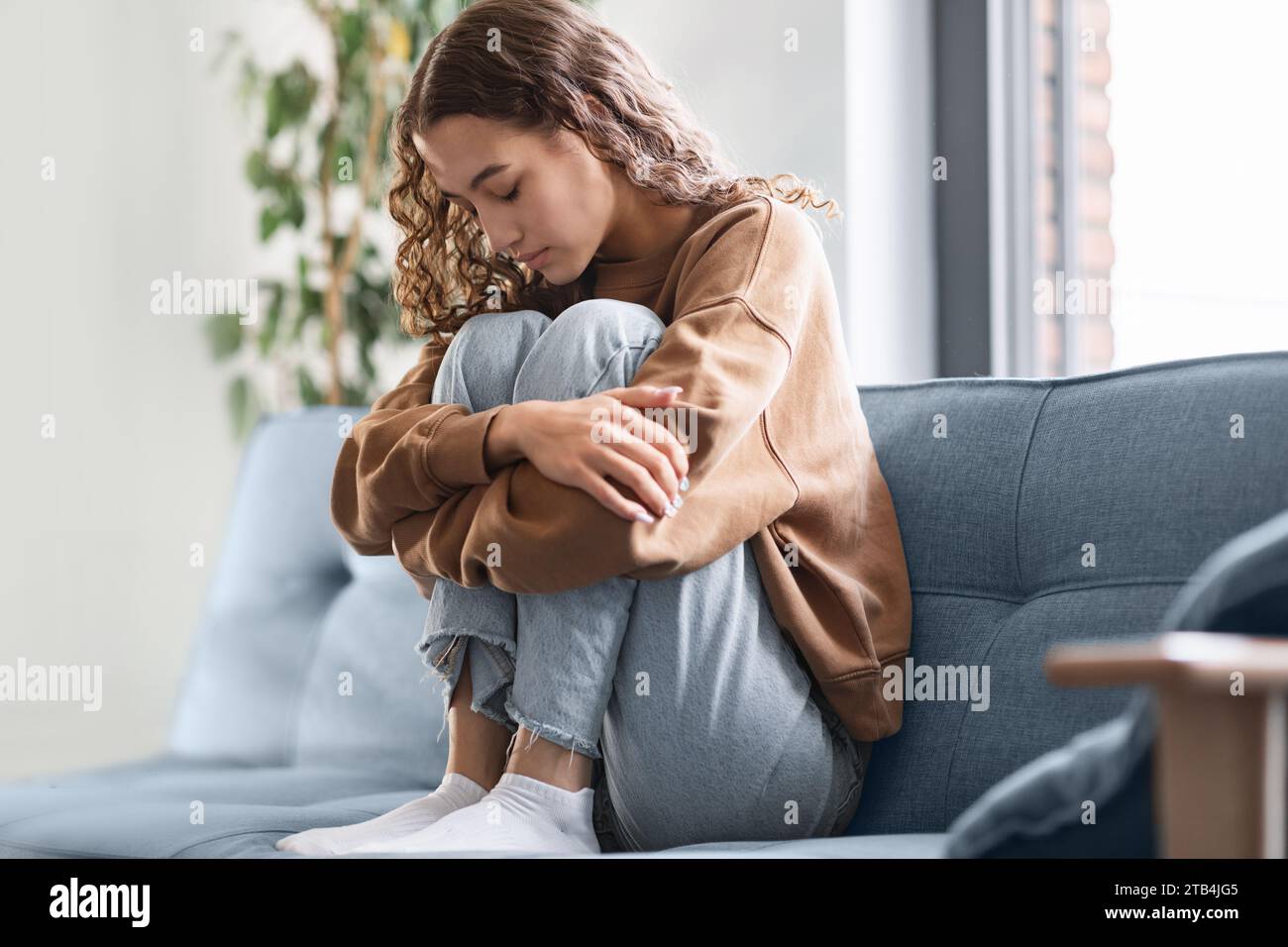 Distressed teenage girl sits on couch at home hugging knees Stock Photo ...