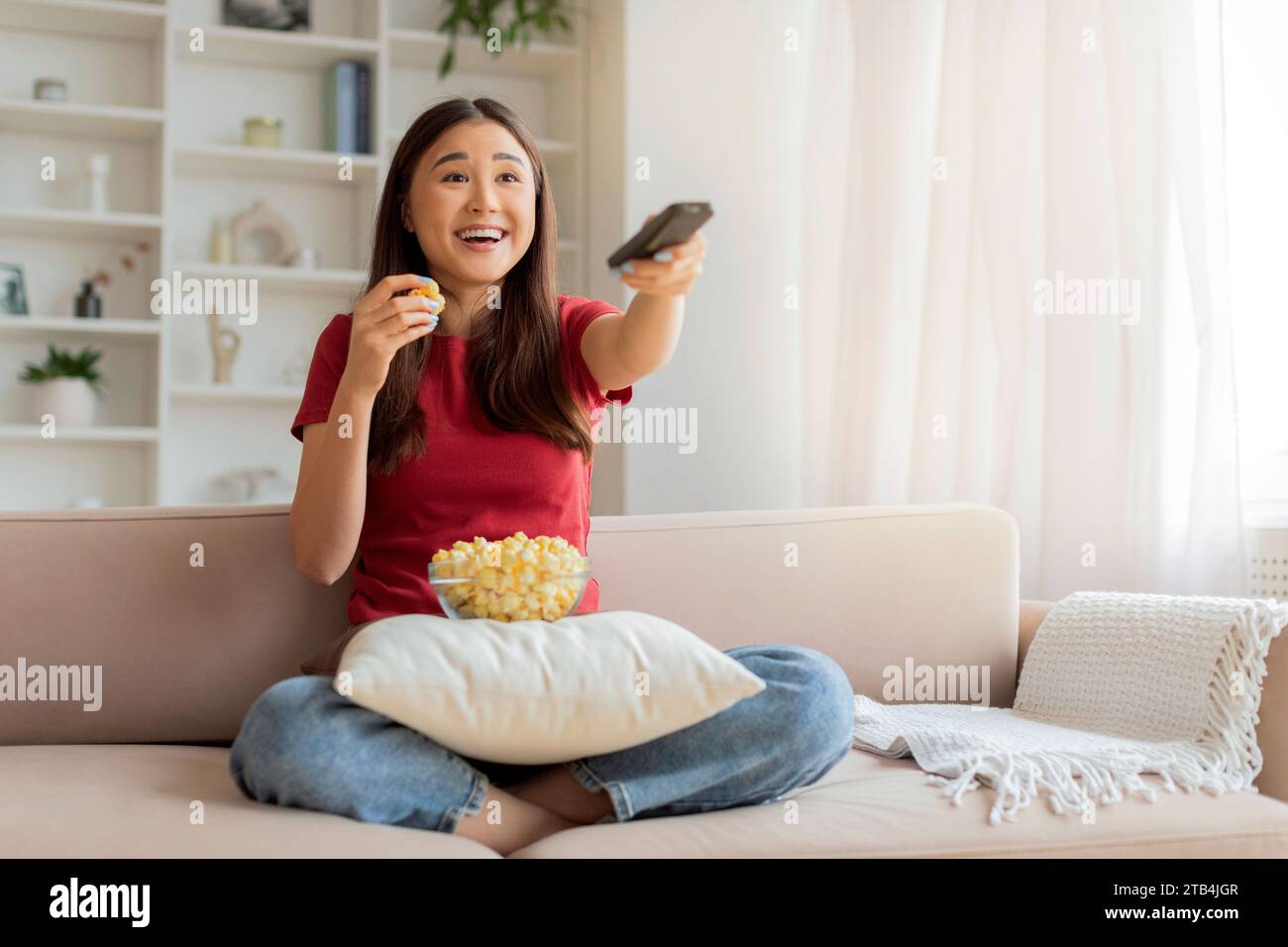 Asian woman switching channels with remote controller while watching TV ...