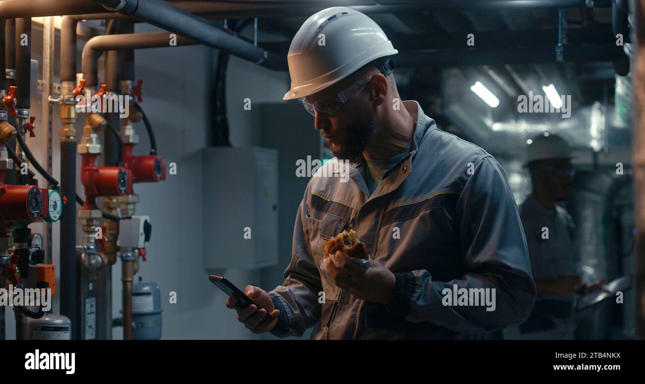 Professional engineer works at modern factory, eats burger and uses ...