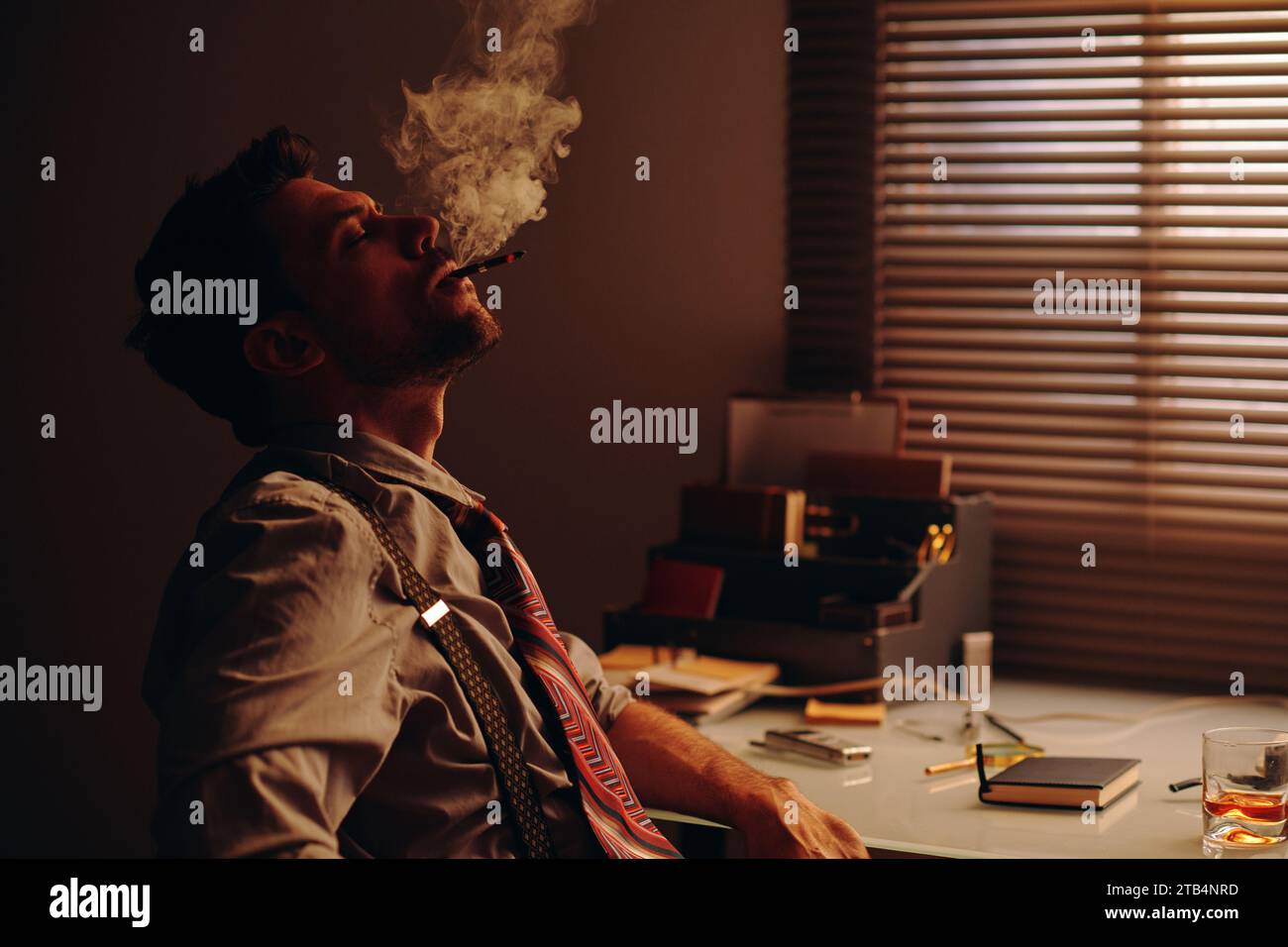 Young relaxed man with cigarette in mouth blowing smoke while sitting ...