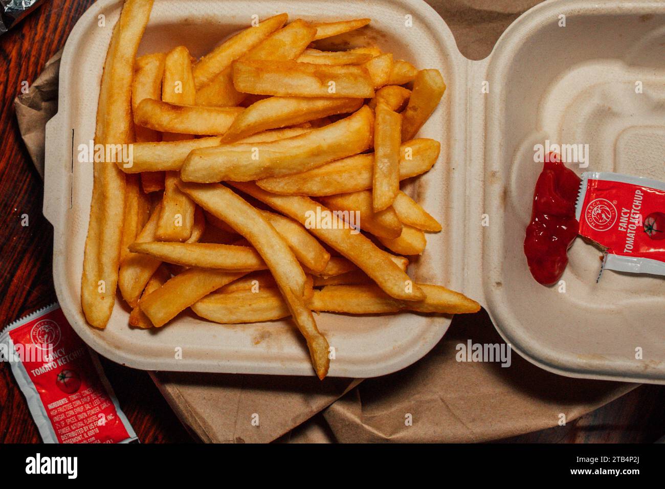 paper box of takeout French fries with packets of "fancy tomato ketchup ...