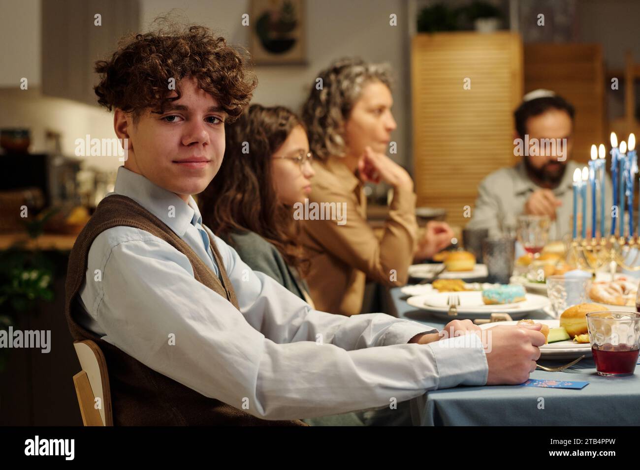 Youthful Jewish boy in casualwear looking at camera by dinner table ...