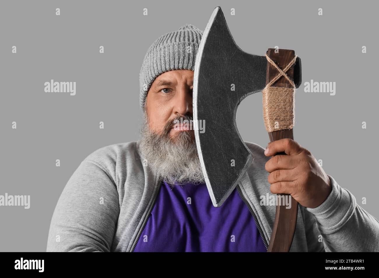 Portrait of mature man covering face with axe on grey background Stock ...