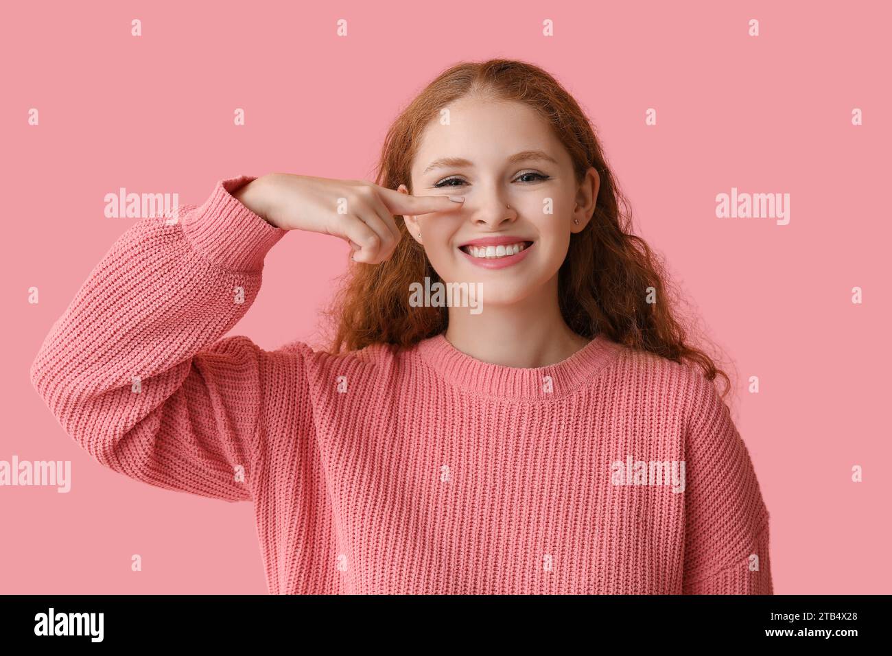 Portrait of pretty young girl pointing at her nose on pink background ...