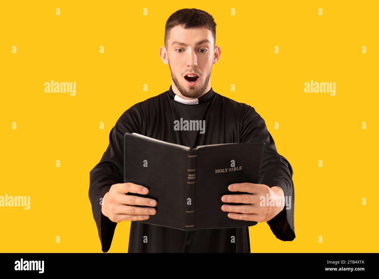 Shocked young priest with Holy Bible on yellow background Stock Photo ...