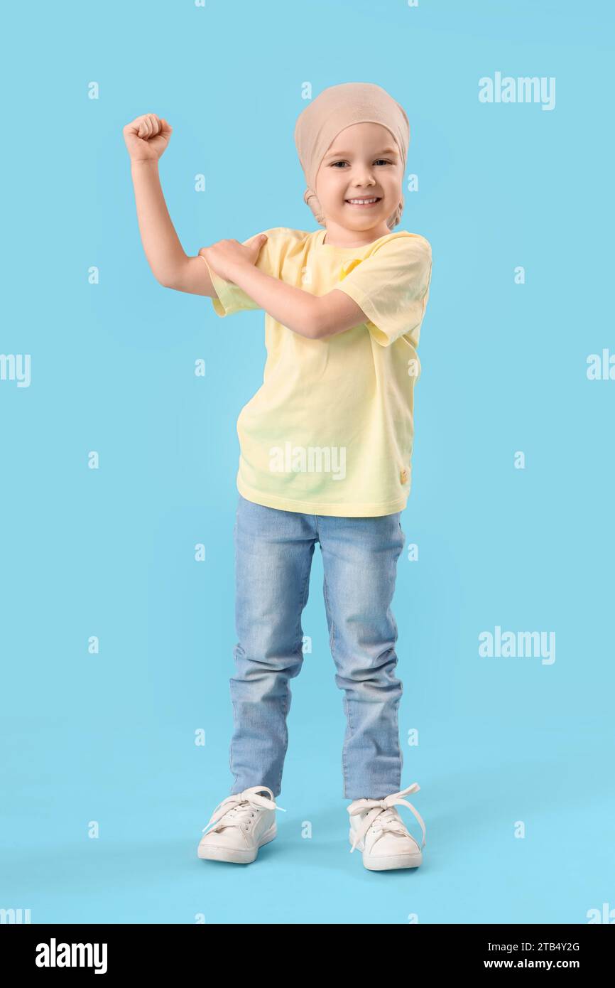 Little girl after chemotherapy showing muscles on blue background ...