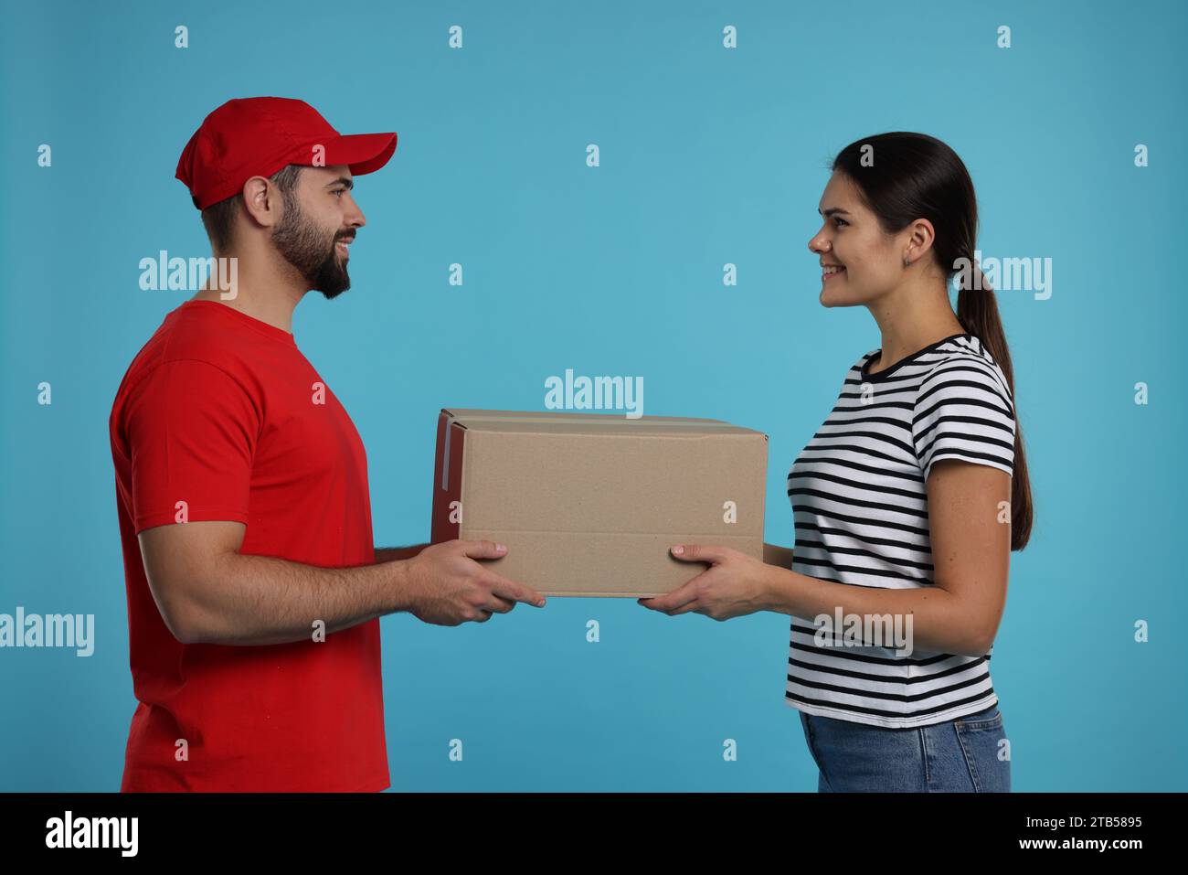 Smiling courier giving parcel to receiver on light blue background ...