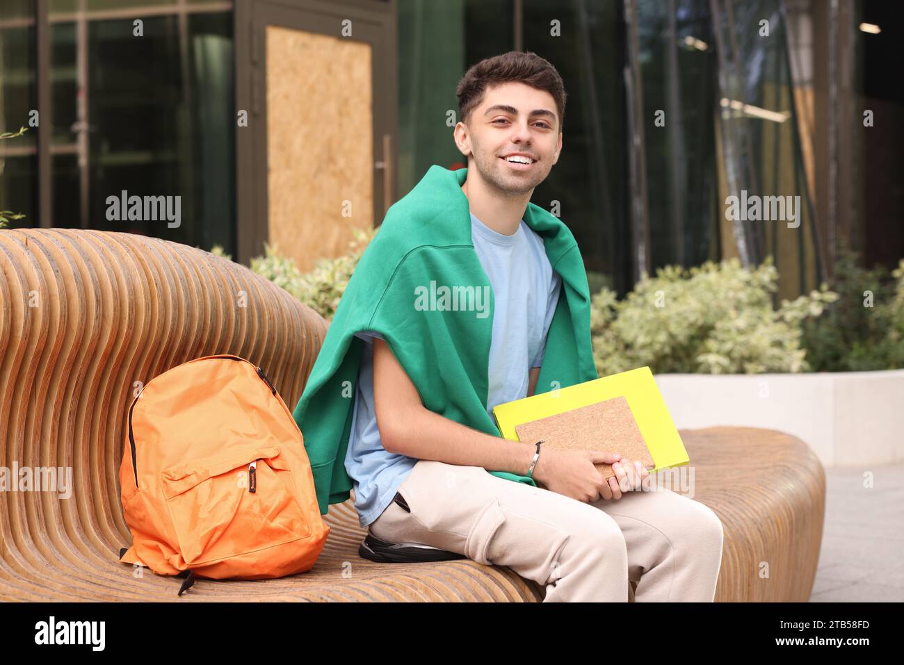 Happy young student with notebooks on bench outdoors Stock Photo - Alamy