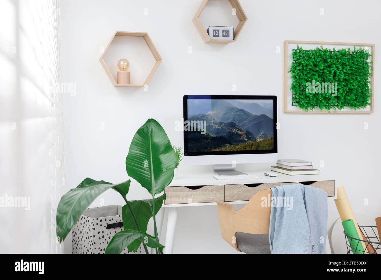 Green artificial plant wall panel and desk with computer in light room ...