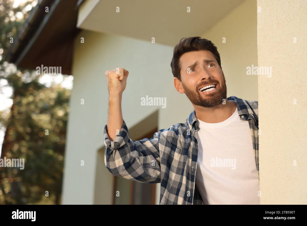 Angry man showing fist near house, low angle view. Annoying neighbour ...