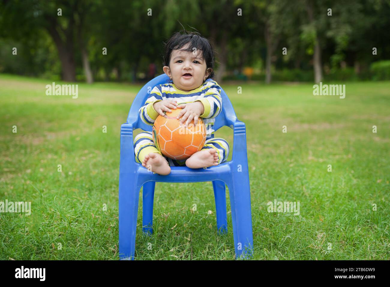 Cute baby boy sitting on blue chair in a garden playing with ball Stock ...