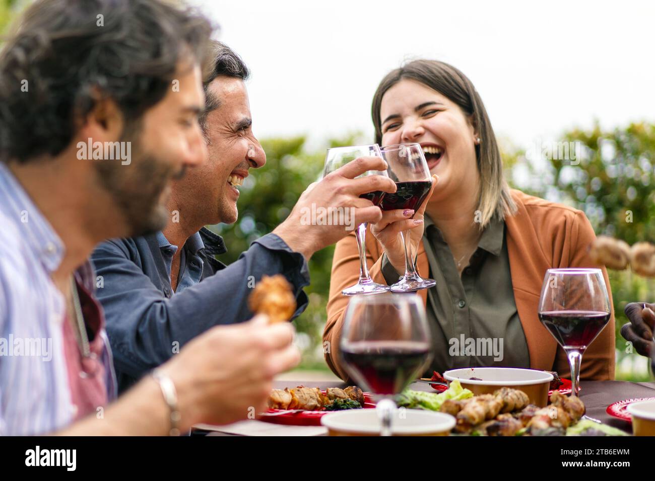 Joyful friends sharing a toast with red wine, laughing over a meal at ...
