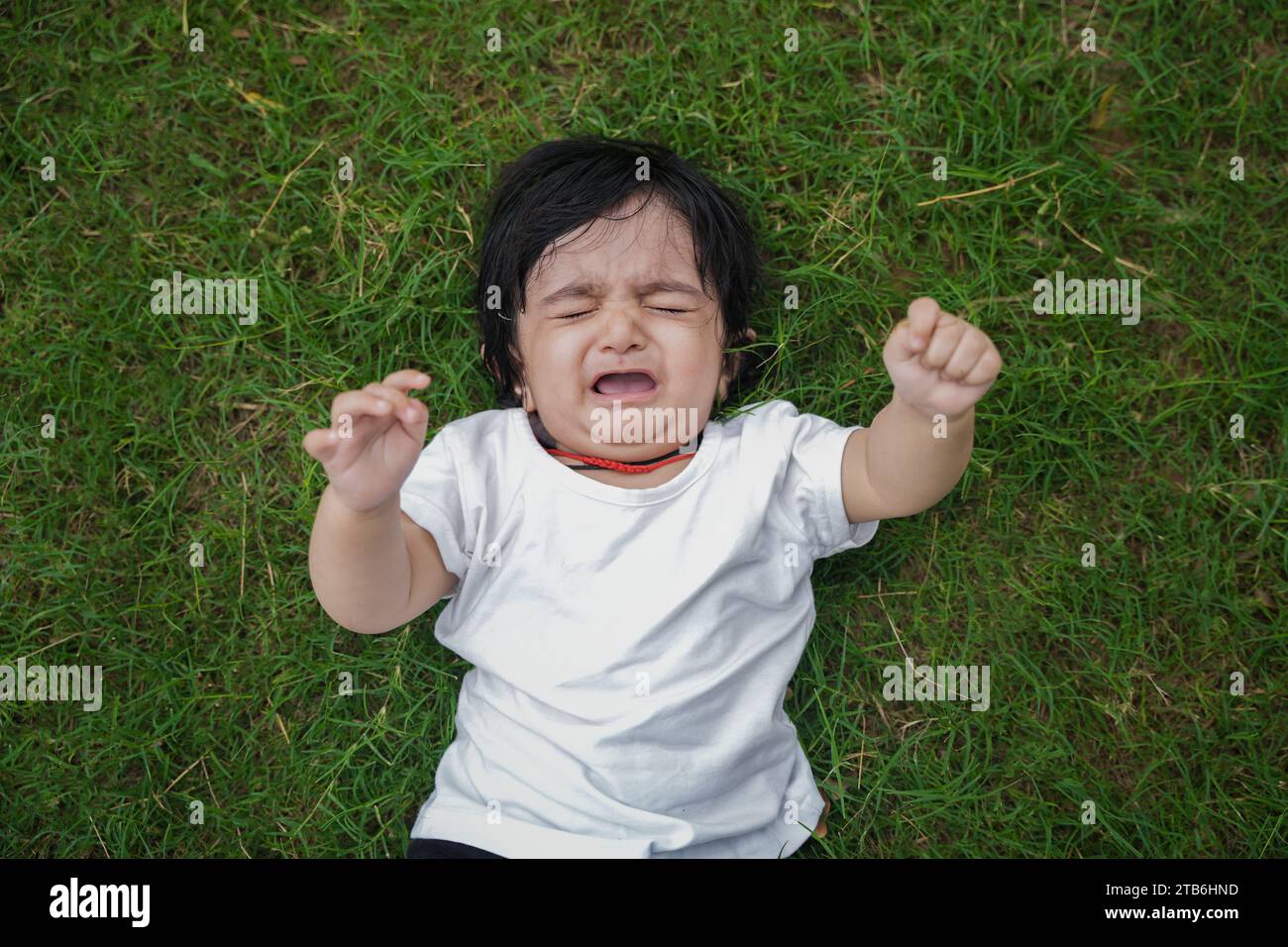 Cute indian boy lying in garden crying Stock Photo - Alamy