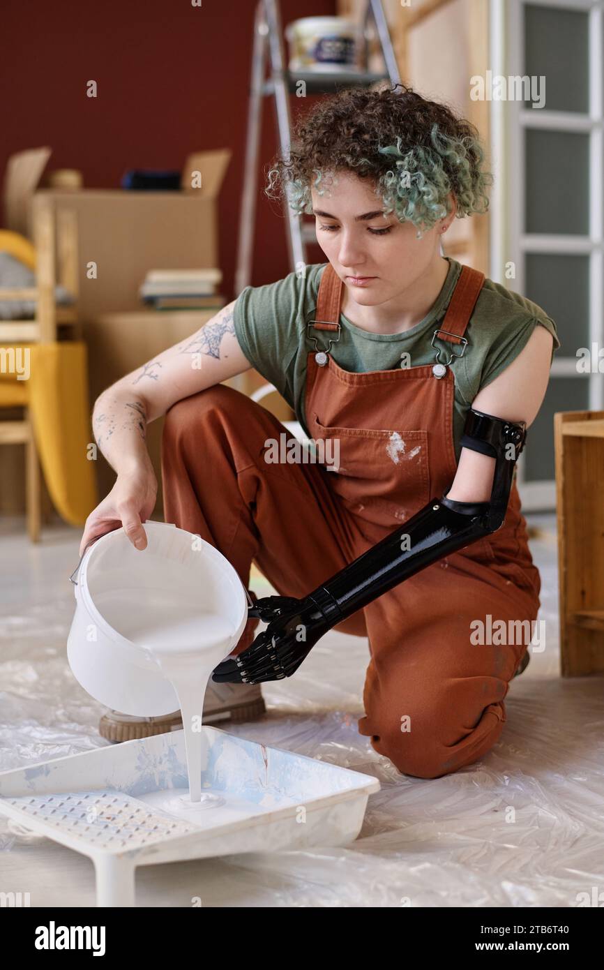 Vertical image of girl with prosthetic arm painting walls in the room ...