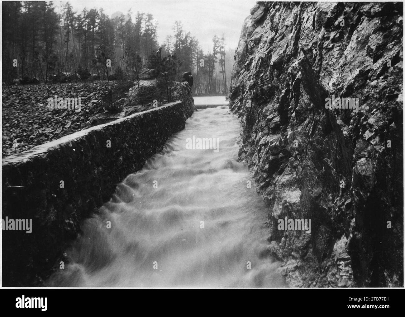 Water overflow rushing between bluff on right and stone wall on left ...