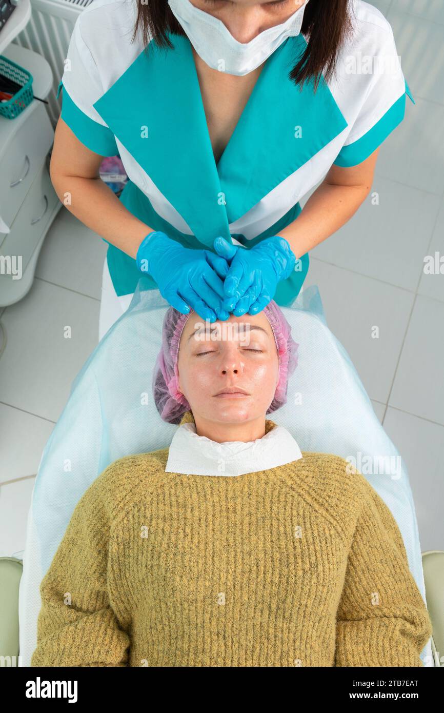 A female cosmetologist manually treats the patient's skin with a ...