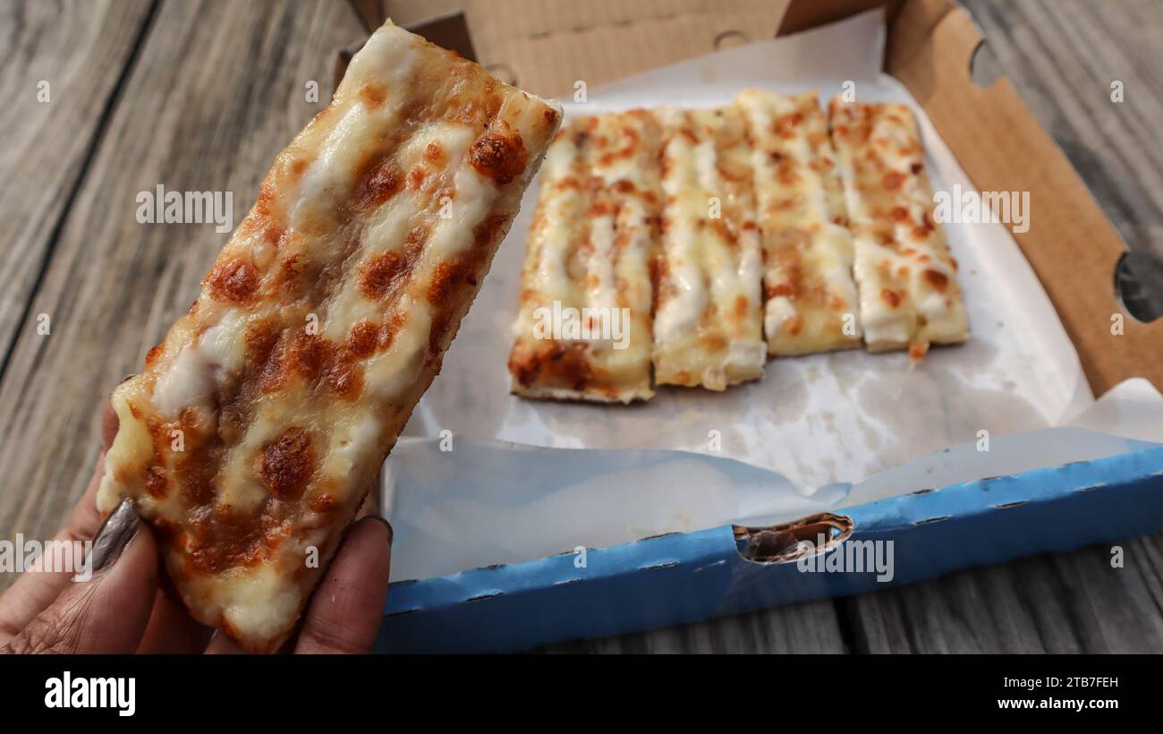 Female holding eating Cheesy garliz Pizza Bread sticks. Baked otem ...