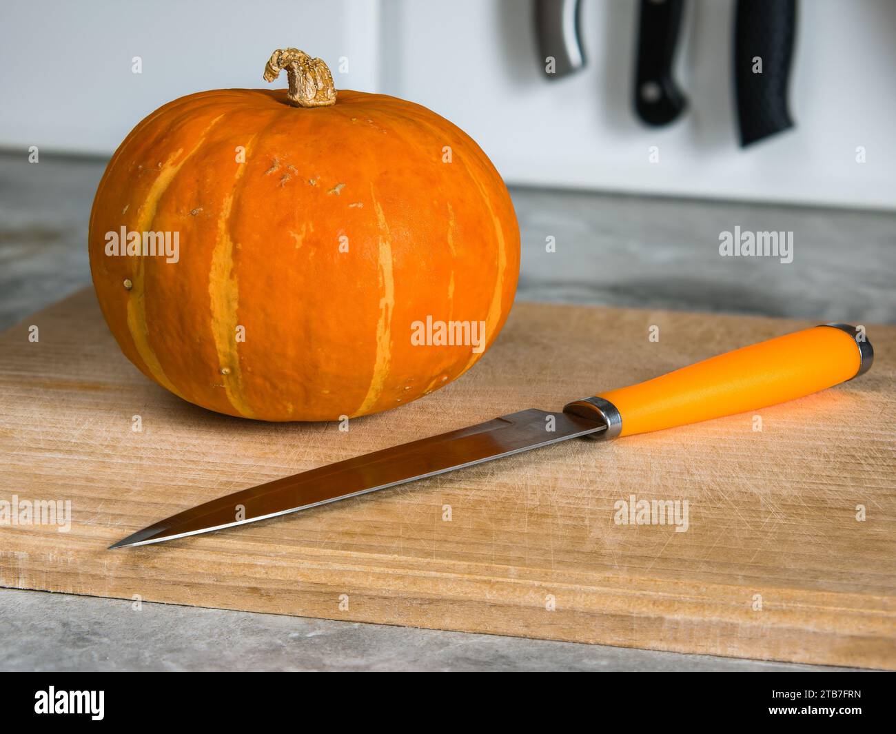 Pumpkin on a rectangular beech cutting board and a knife with an orange ...