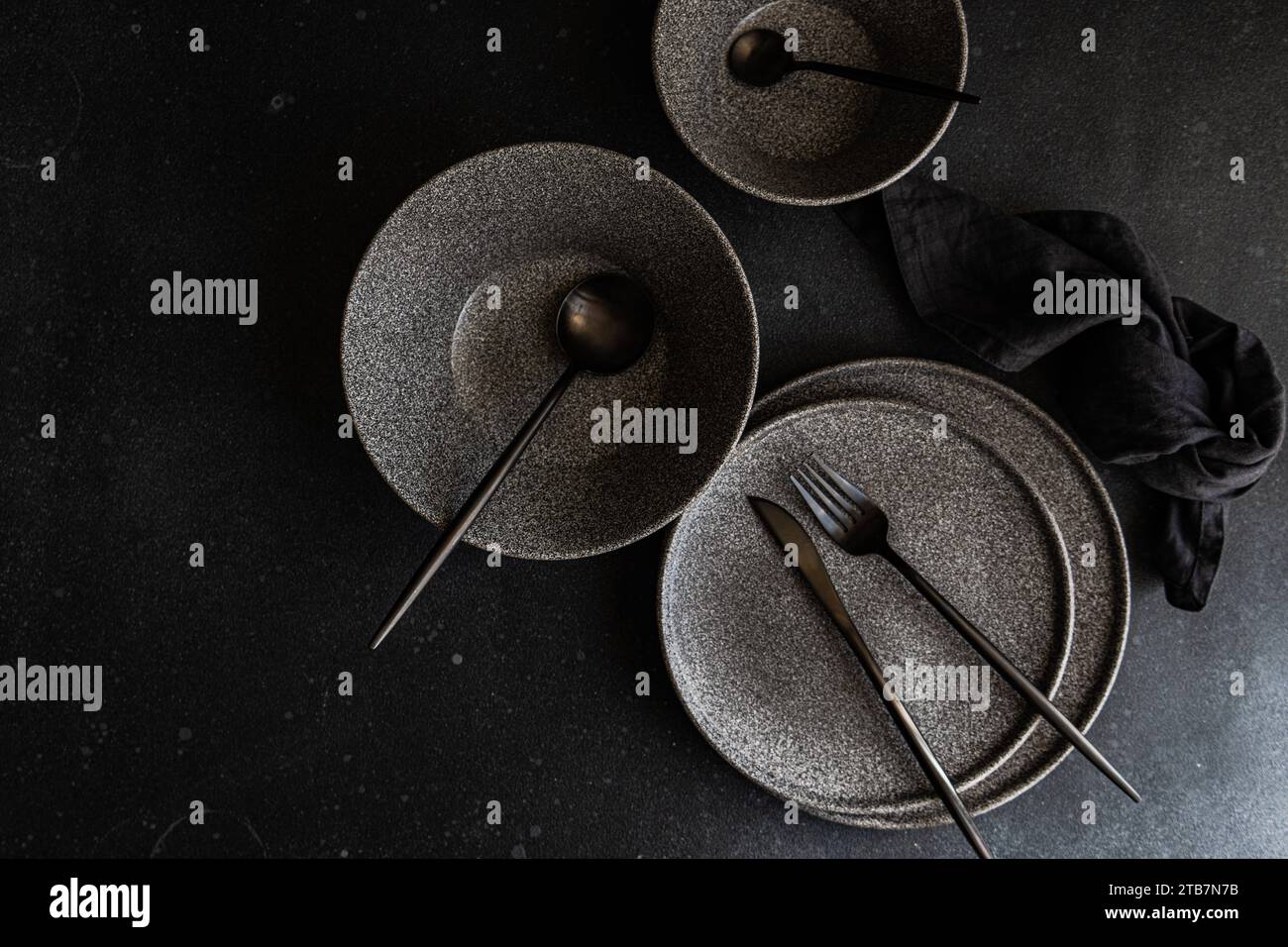 An aesthetic arrangement of dark stoneware dishes with a rustic charm, set on a dark textured ...