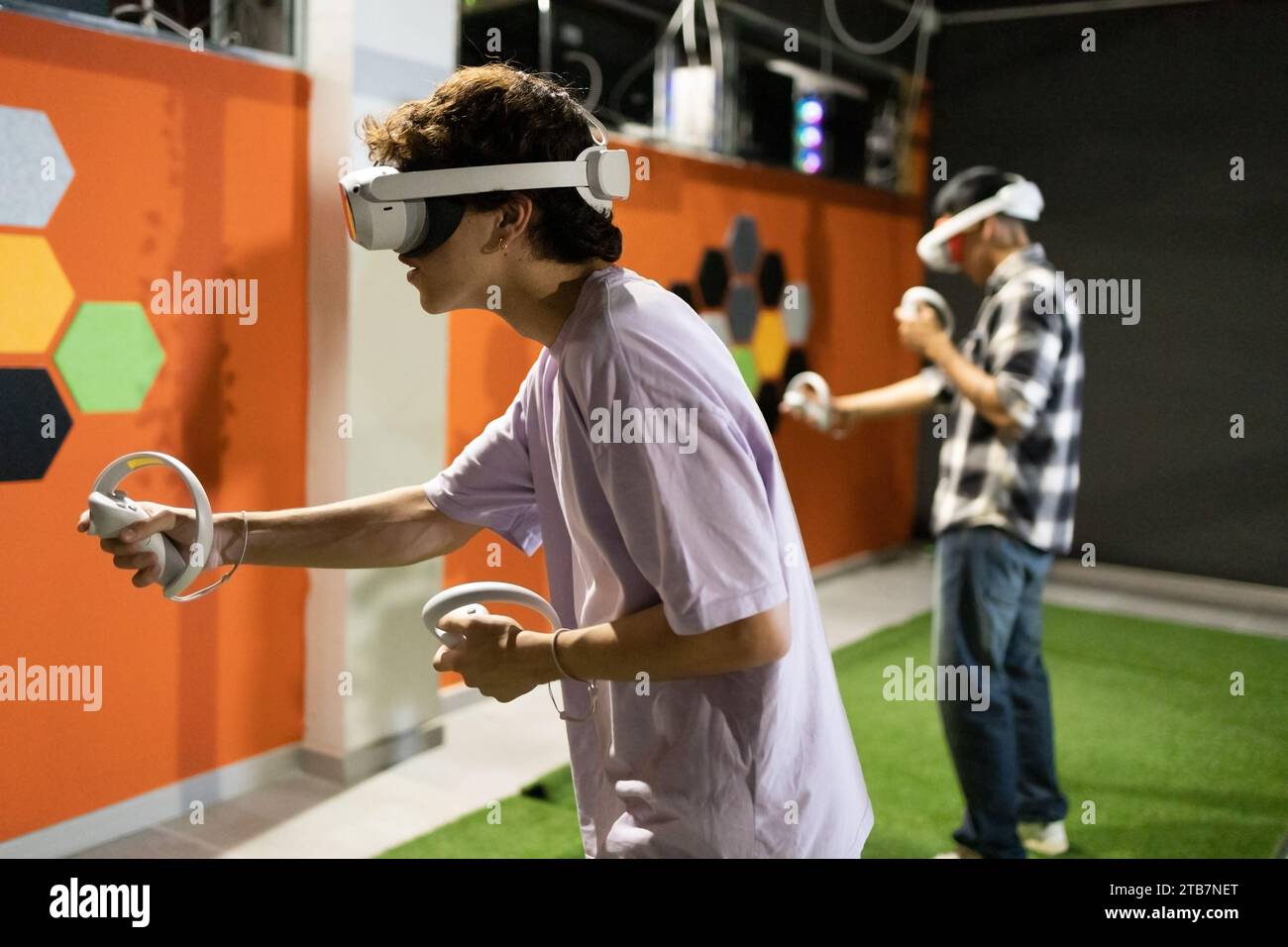 Side view of two friends stand in a gaming area fully immersed in a ...