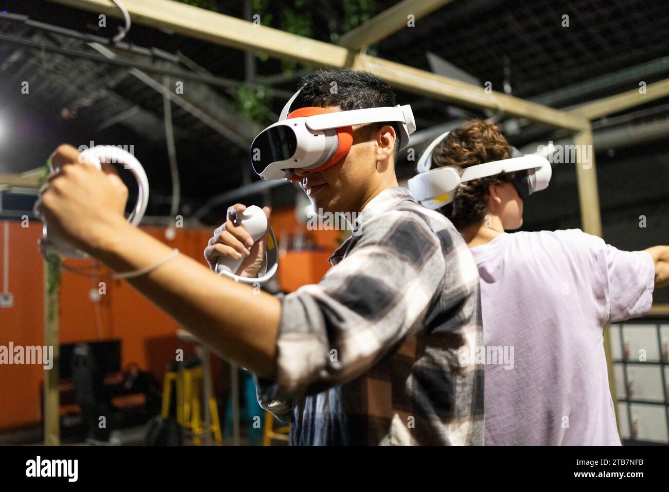 Side view of two friends stand in a gaming area fully immersed in a ...